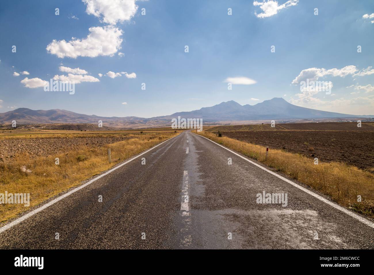 Long straight road going across countryside, leading to mountains far ...