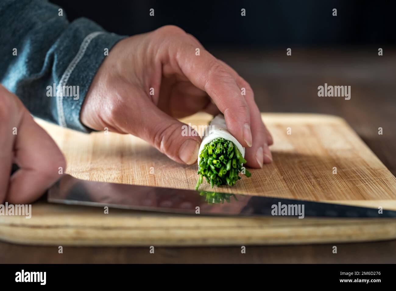 a bundle of chives in a roll ready for slicing, on a wooden cutting ...