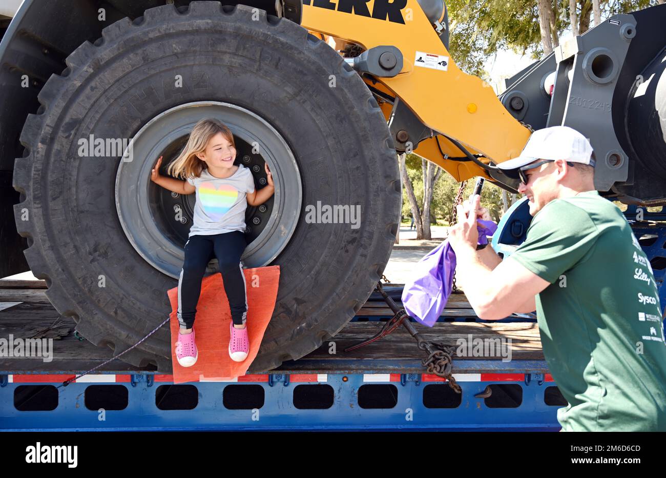 A child smiles for a photo while sitting in the wheel of a large ...