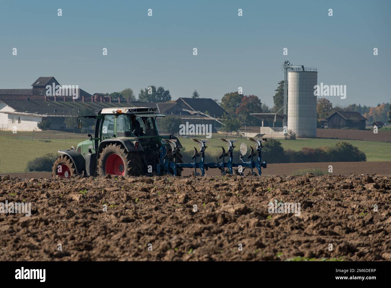 Tractor ploughing a field with blurry farm in the background Stock ...