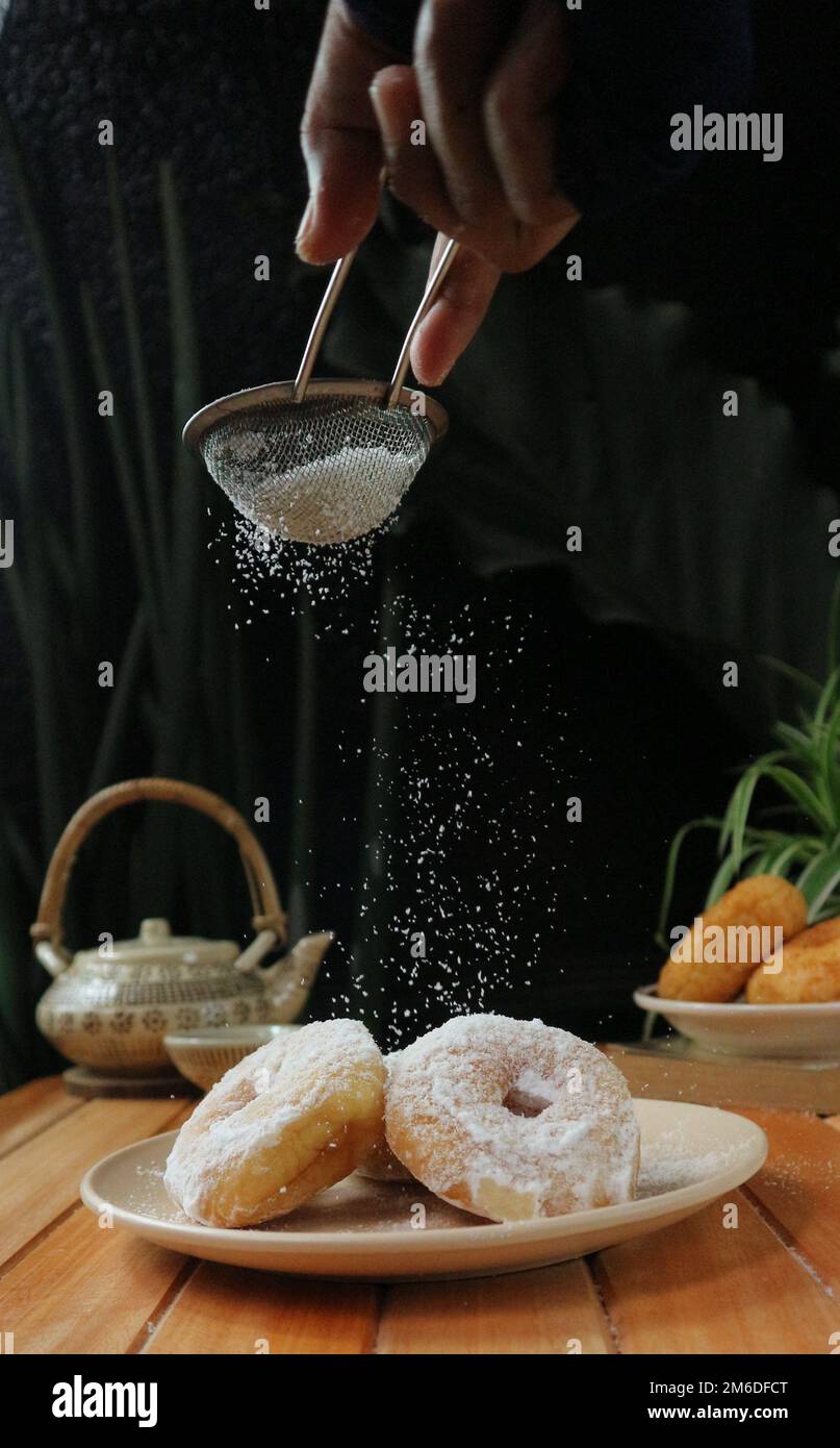 Sprinkle white sugar on donuts Stock Photo - Alamy