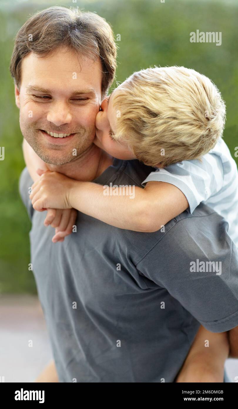 Love of a son. Young boy kisses his fathers cheek while he gives him a ...