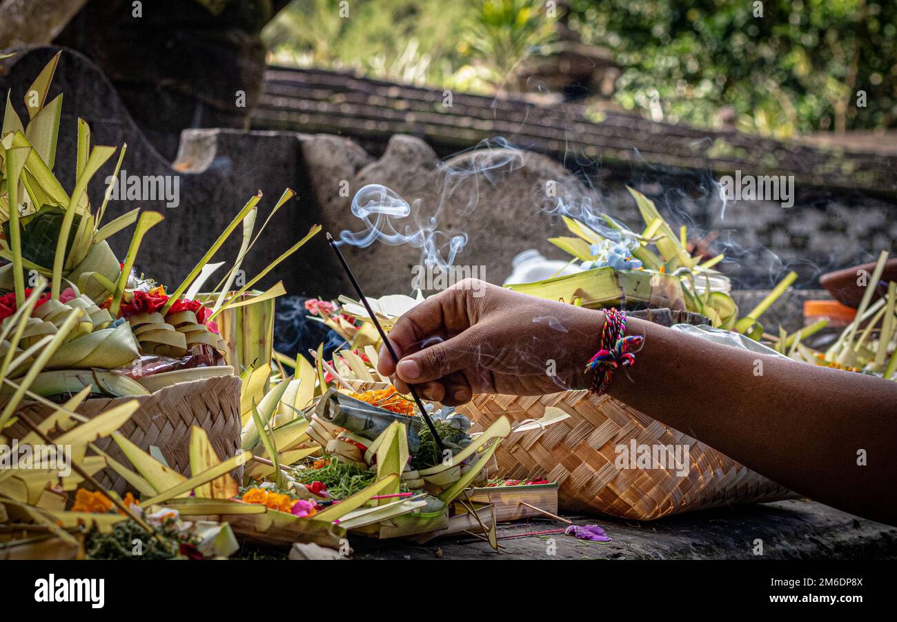 A hand placing burning incense in an offering at a Balinese temple ...