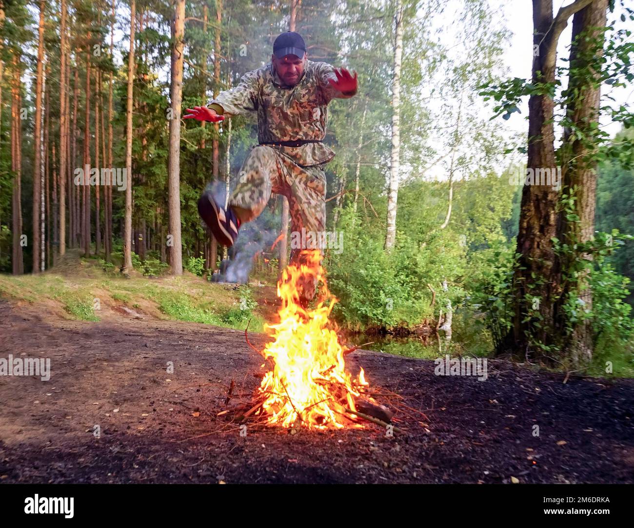A young man in a jump over a burning fire on the lake shore Stock Photo ...