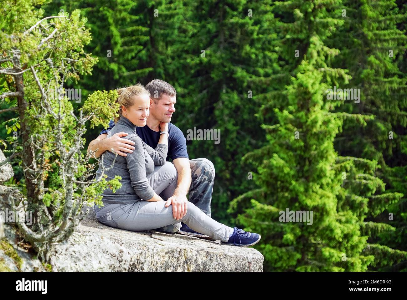 A man and a woman sit hugging each other on the edge of a mountain in ...