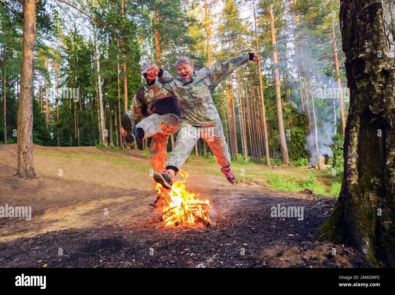 Elderly man and woman in a jump over a burning fire on the lake shore ...