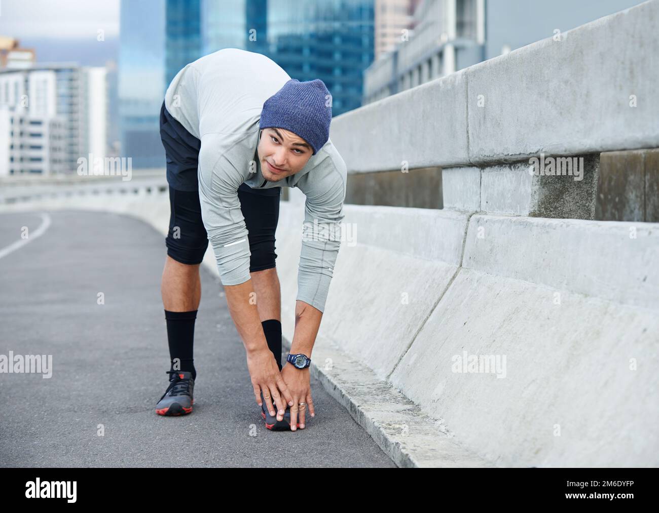 Last stretch before the run. Portrait of a young male jogger stretching ...