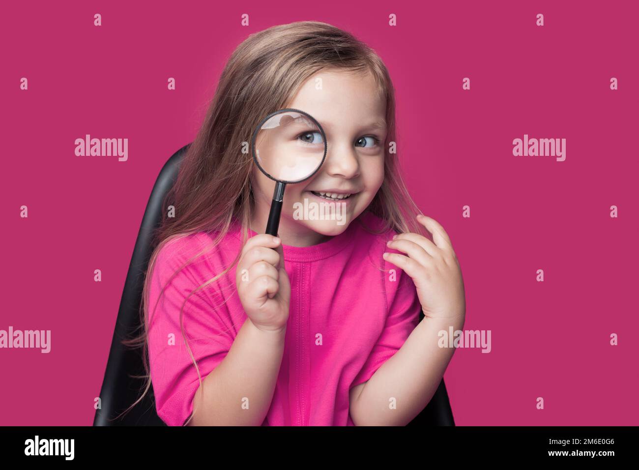 Little girl sitting on chair, holding magnifying glass and looking at ...
