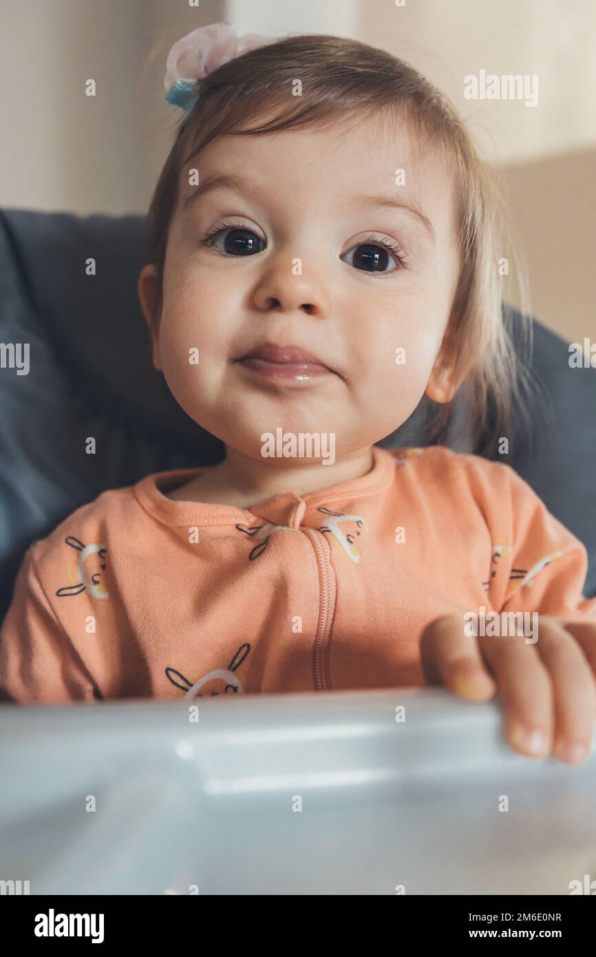 Close-up portrait of baby girl sitting on a high chair ready to eat ...