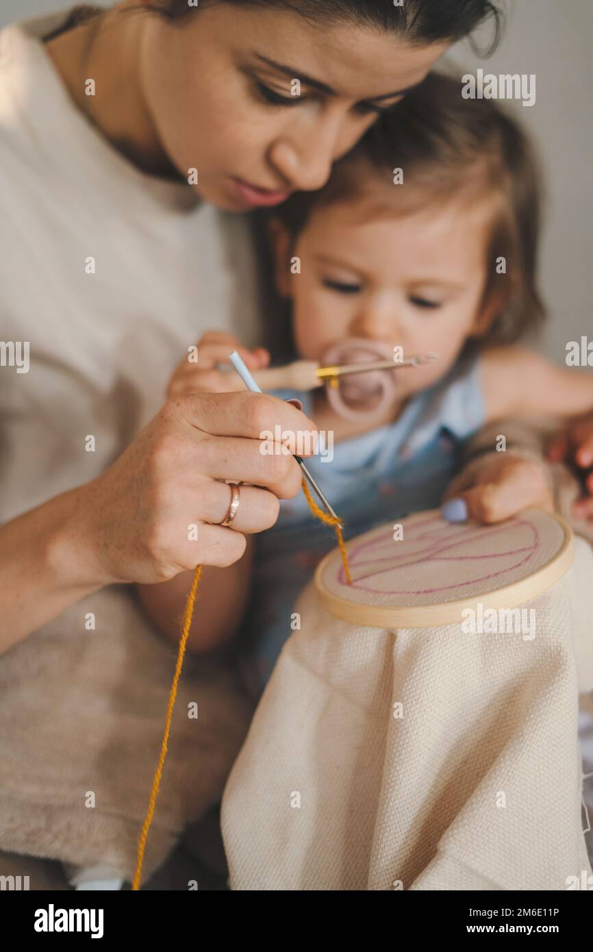 Mother teaching baby daughter embroidery technique. Close up portrait ...