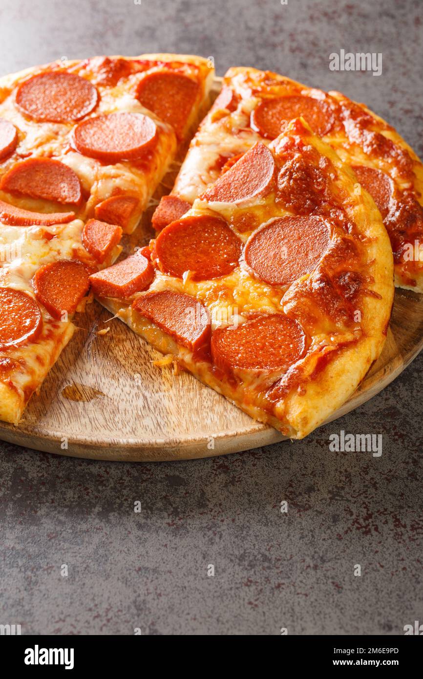 Homemade pepperoni pizza with sausage, cheese and tomato sauce close-up on a wooden board on the ...