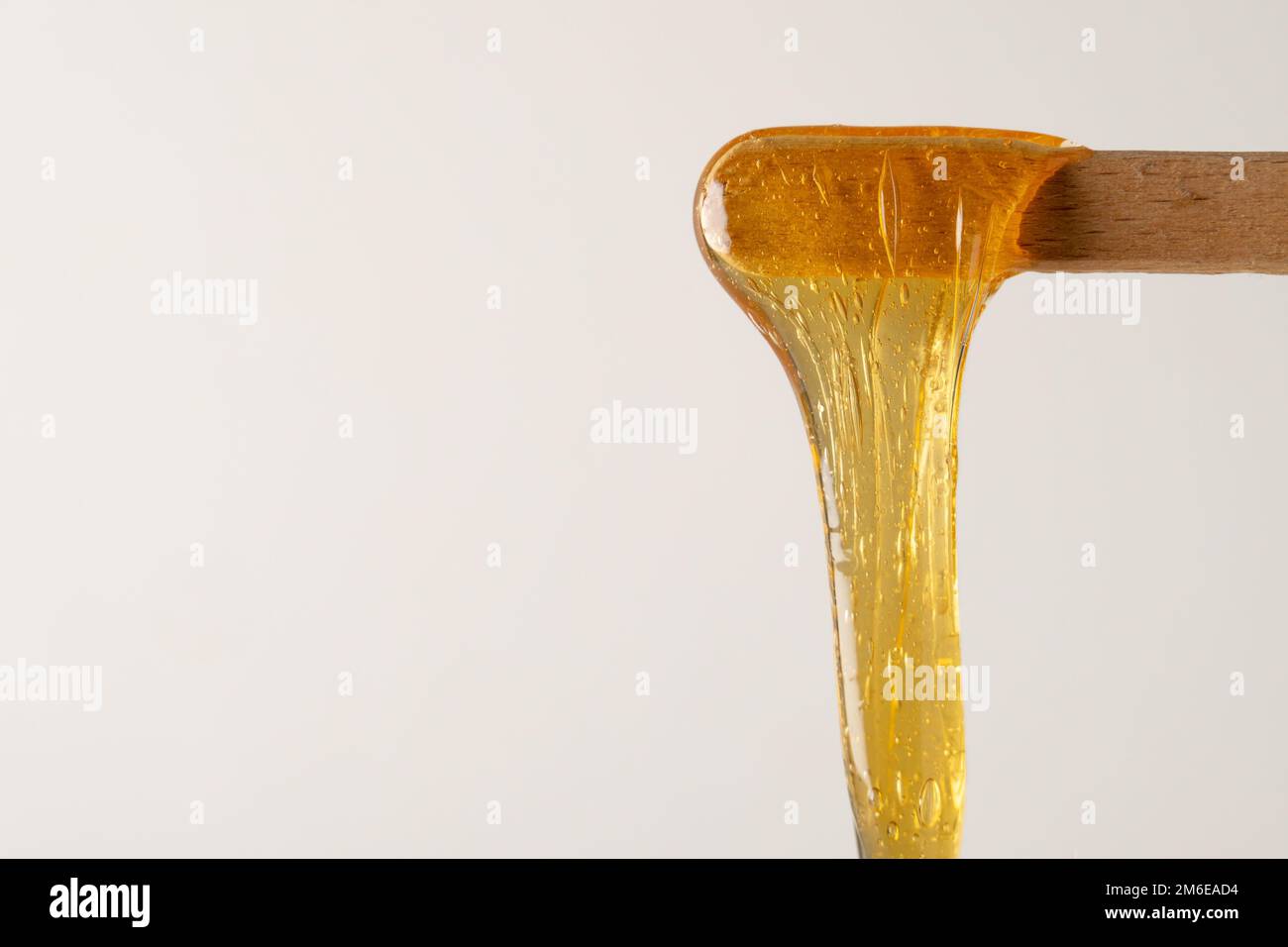 Liquid yellow sugar paste or wax for epilation on wooden stick or ...