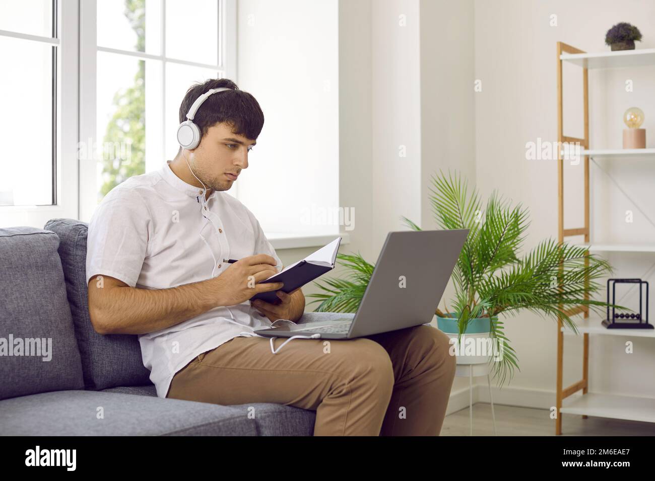 Young man sitting on couch, studying online, looking at laptop computer ...