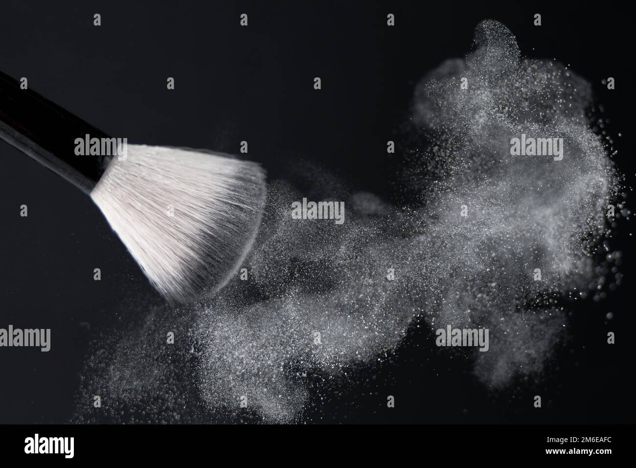 Makeup brush with crushed white floating powder on black background ...