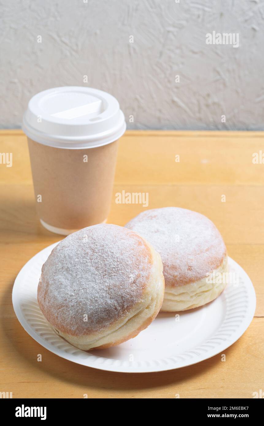 Two donuts on a paper plate and coffee cup on wooden table. Take-away ...