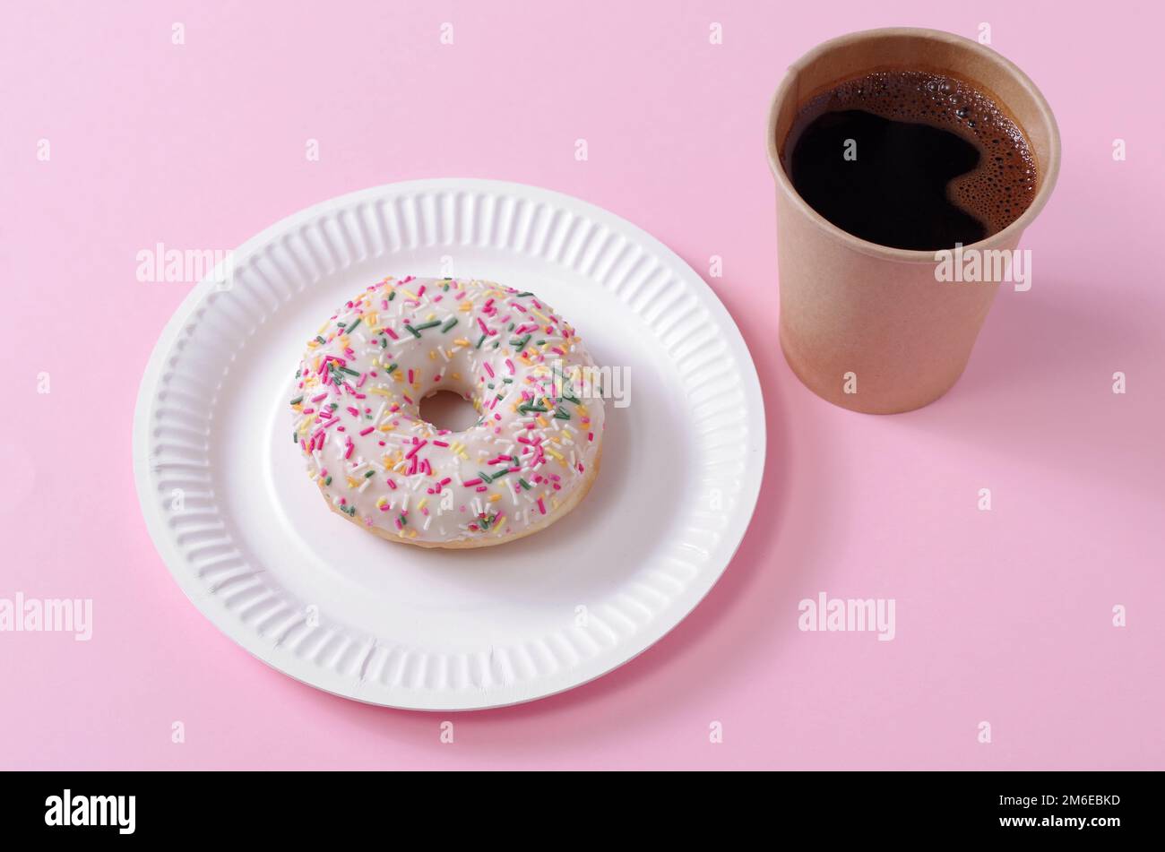 Disposable cup of coffee and donut on a paper plate on pink background ...