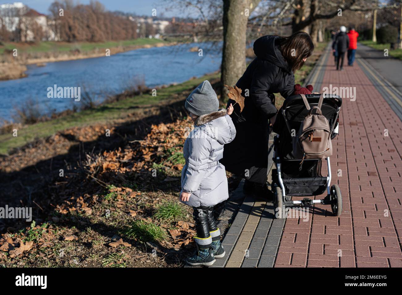 Young woman walking through city park with baby stroller. Warm autumn ...