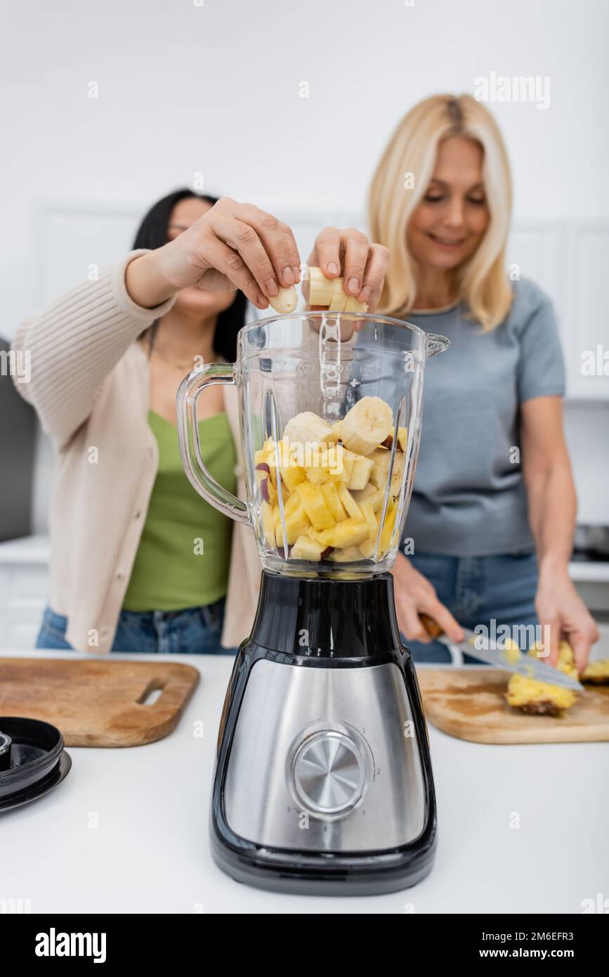 Blurred women cutting and pouring fruits in blender while making ...