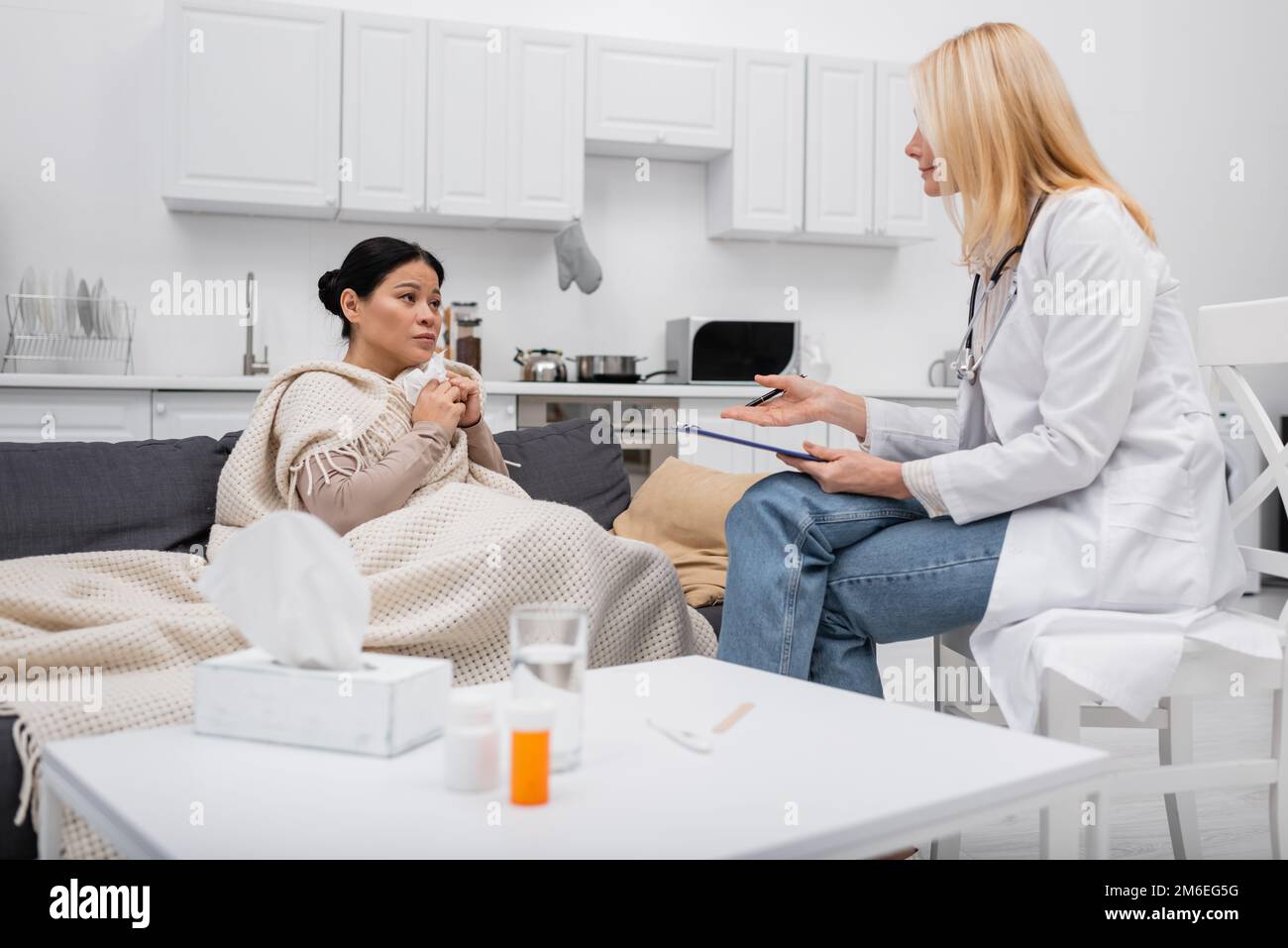 Mature doctor with clipboard pointing at sick asian patient at home ...