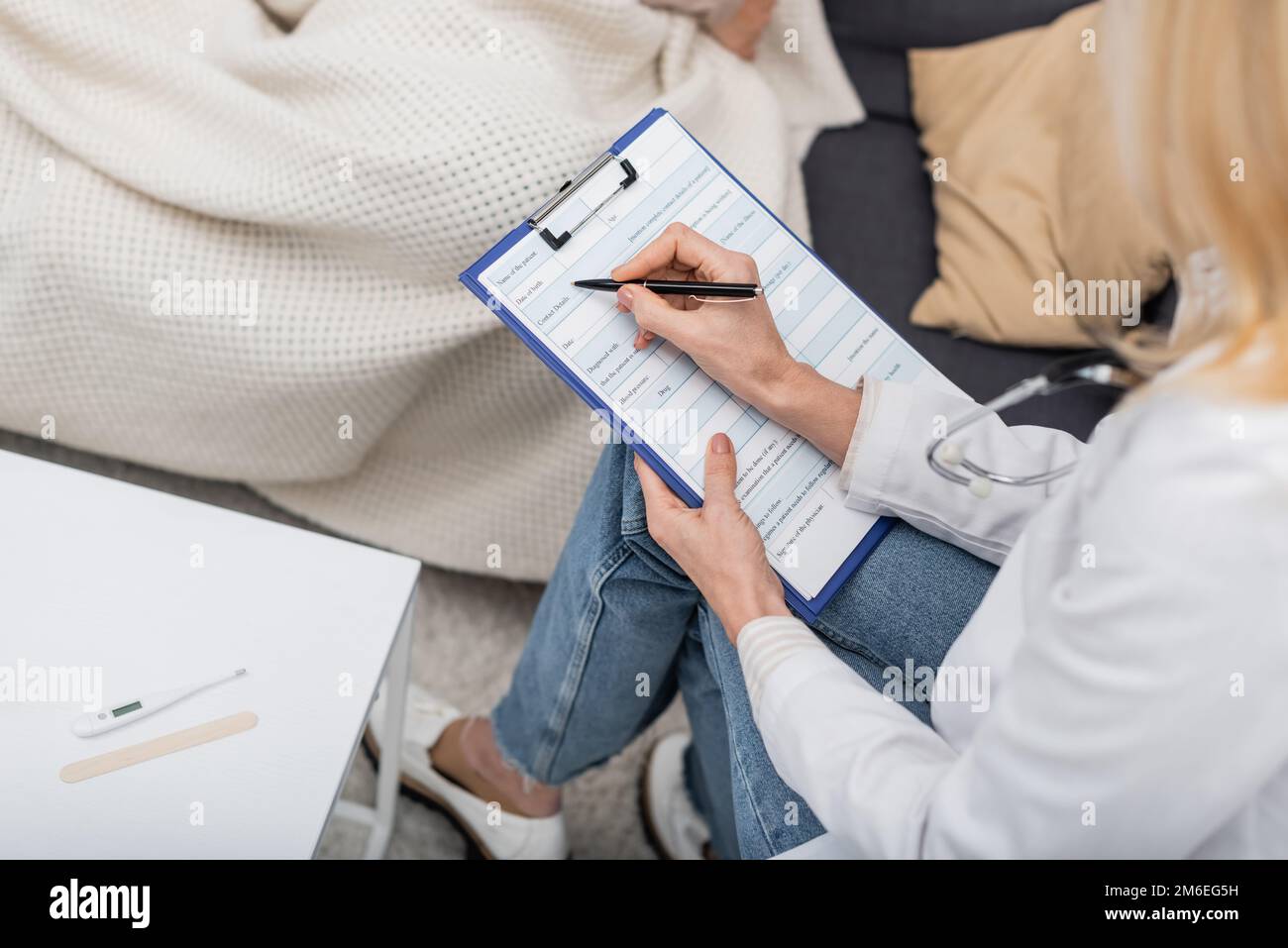 Cropped view of doctor writing on clipboard near electronic thermometer ...