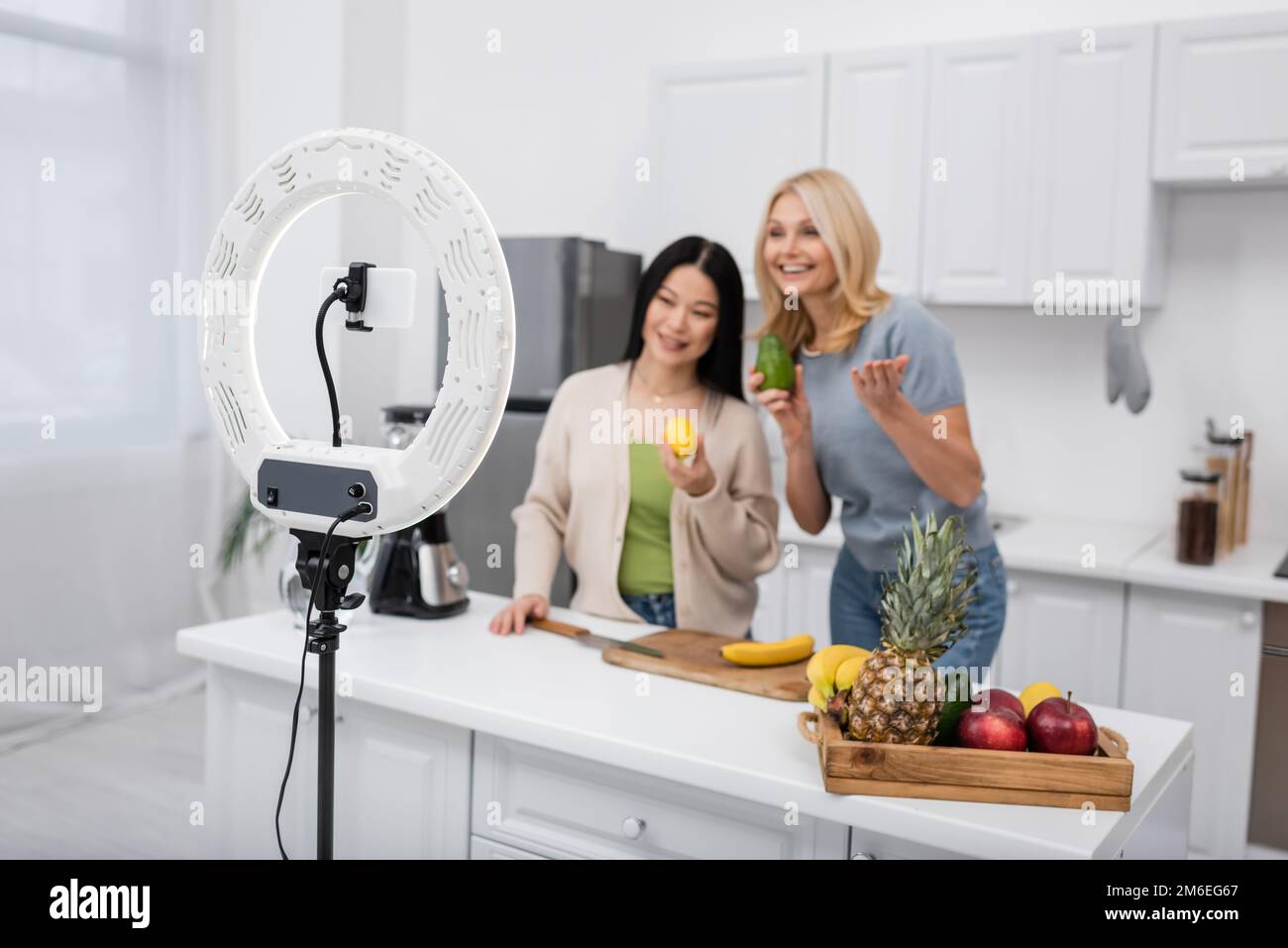 Ring lamp and smartphone near blurred interracial bloggers with ripe ...