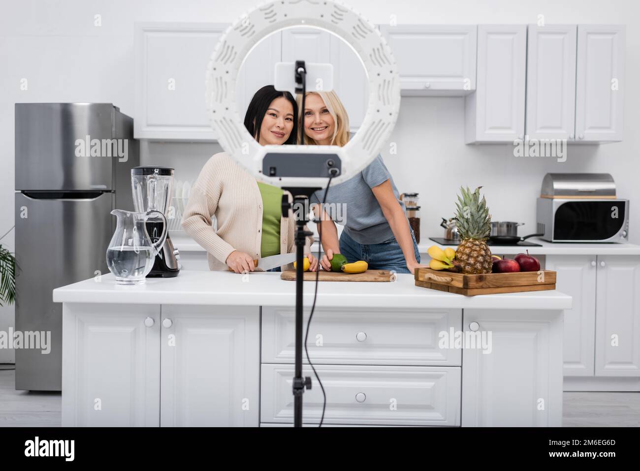 Positive interracial bloggers looking at smartphone in ring lamp near ...