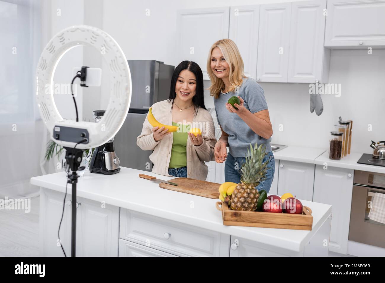 Multiethnic bloggers holding organic fruits near smartphone and ring ...
