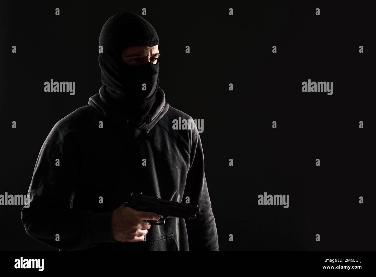 The robber in a mask with a gun pointed to the side on a black ...