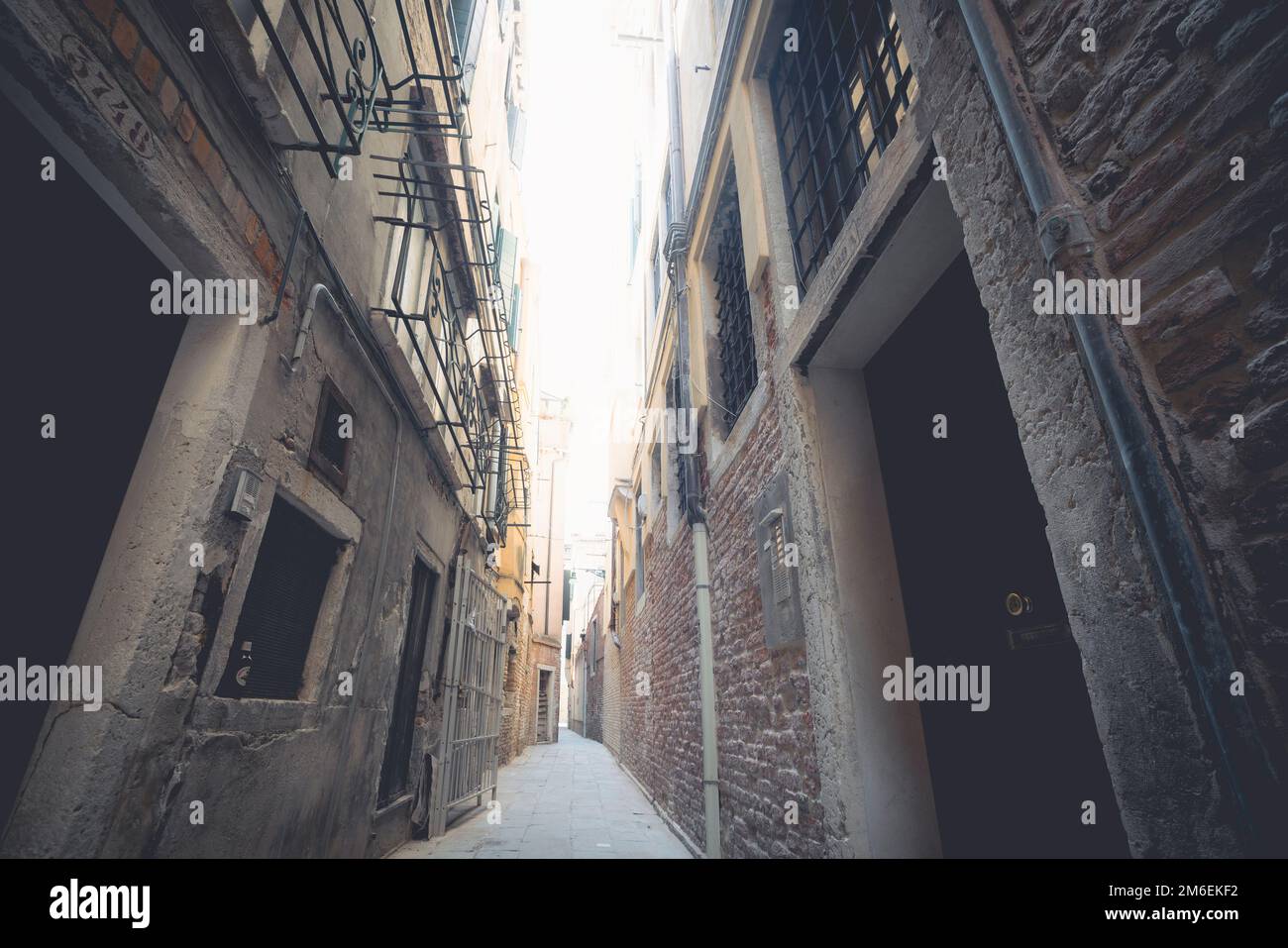 Small alley passage in Venice Italy with tall grunge buildings and bars ...