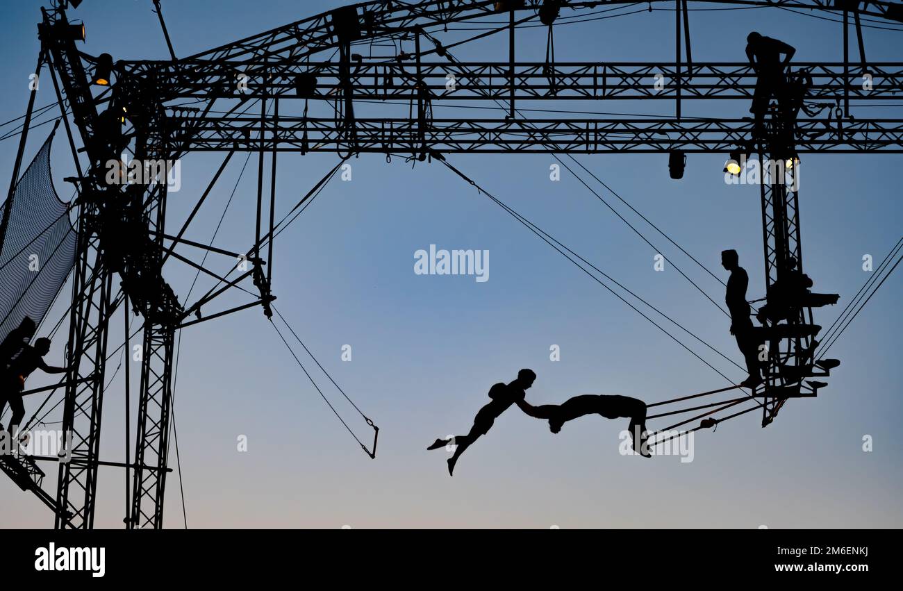 silhouettes of trapeze artists acrobats on the metal scaffolding at ...