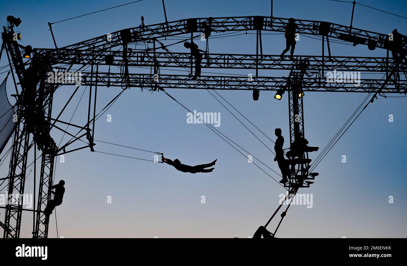 silhouettes of trapeze artists acrobats on the metal scaffolding at ...
