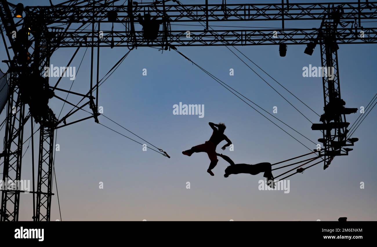 silhouettes of trapeze artists acrobats on the metal scaffolding at ...