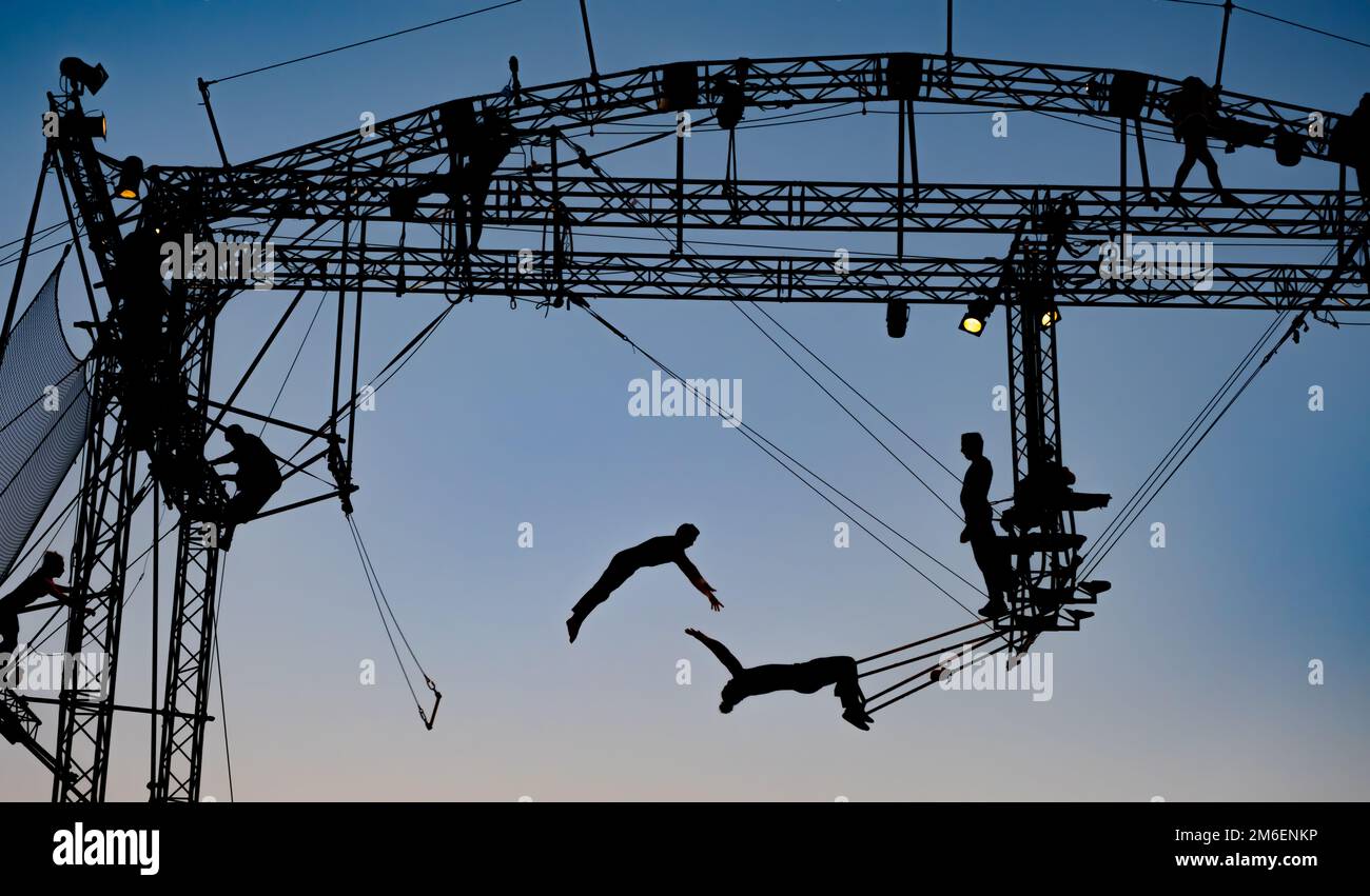 silhouettes of trapeze artists acrobats on the metal scaffolding at ...