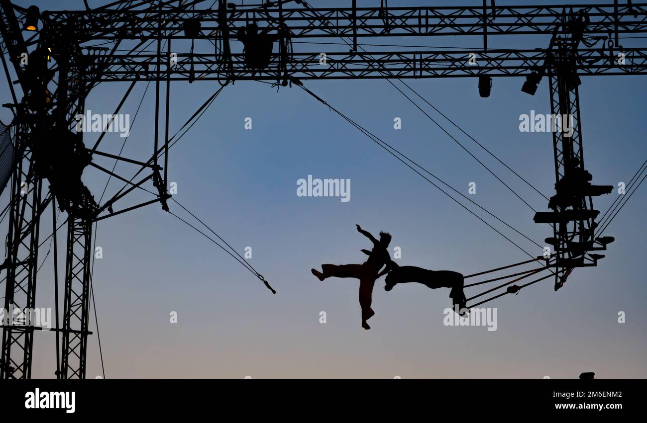 silhouettes of trapeze artists acrobats on the metal scaffolding at ...