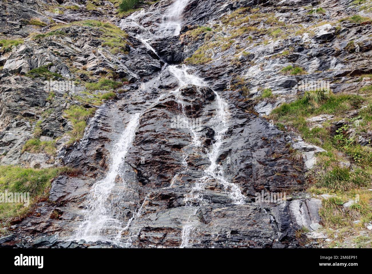 Granite alpine rocks along which a small mountain waterfall flows and ...
