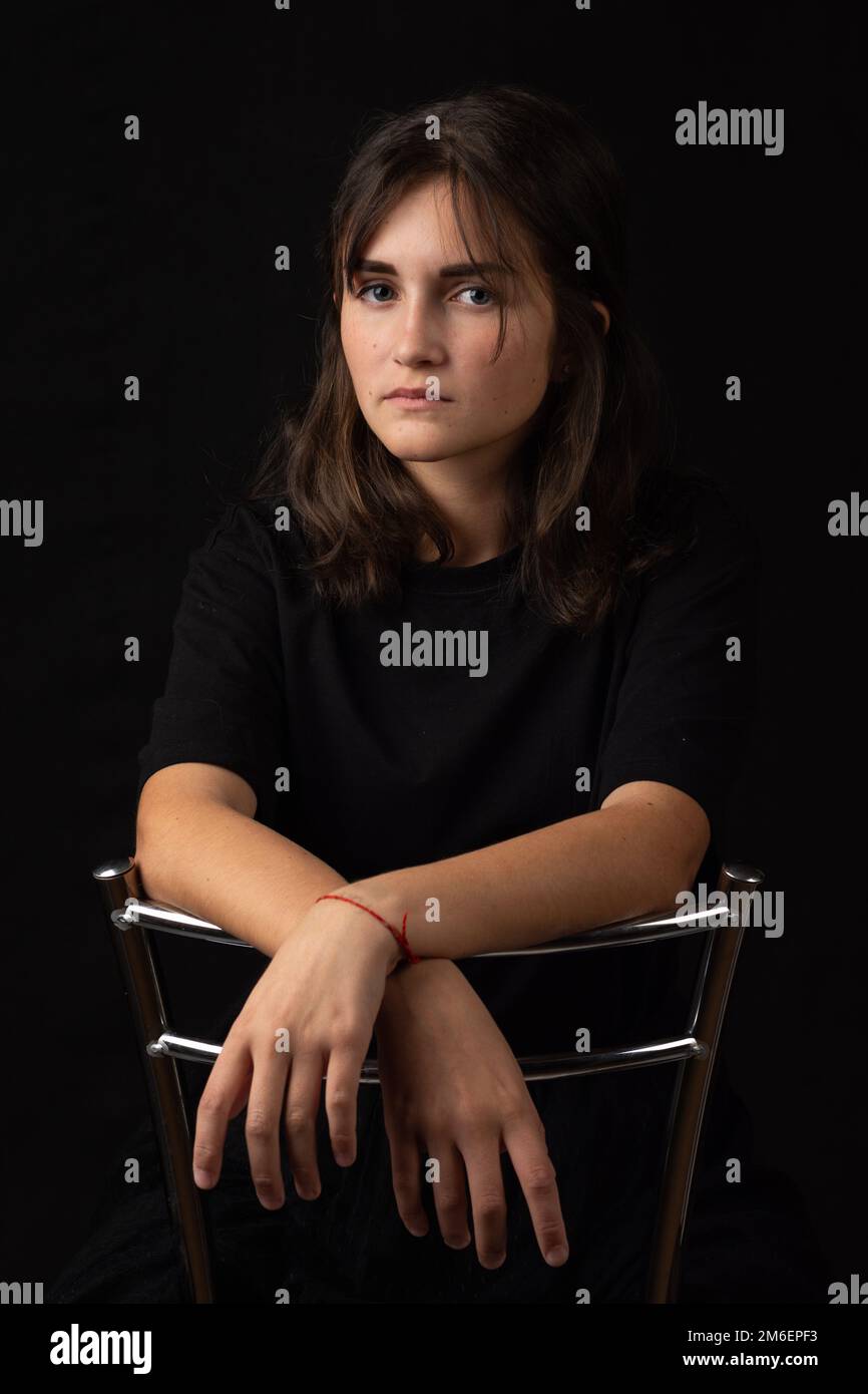 Portrait of a young girl sitting on a high chair with her hands folded ...