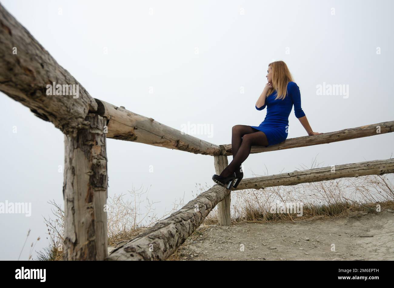 The girl sits on a wooden fence, there is a solid fog around the girl ...