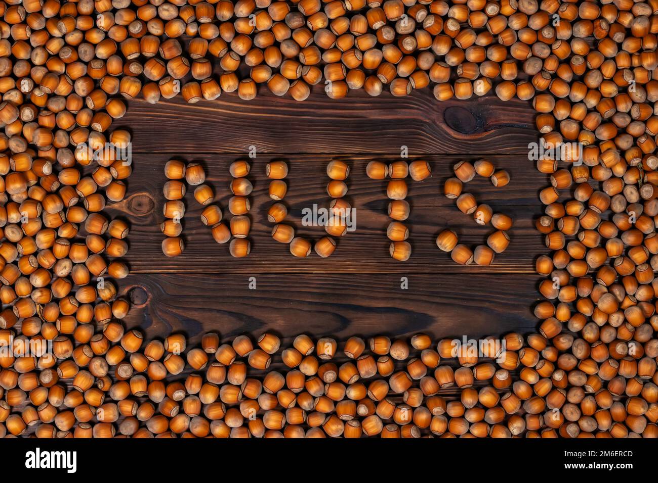 Frame of hazelnuts with shells on brown wooden boards. The word nuts is ...