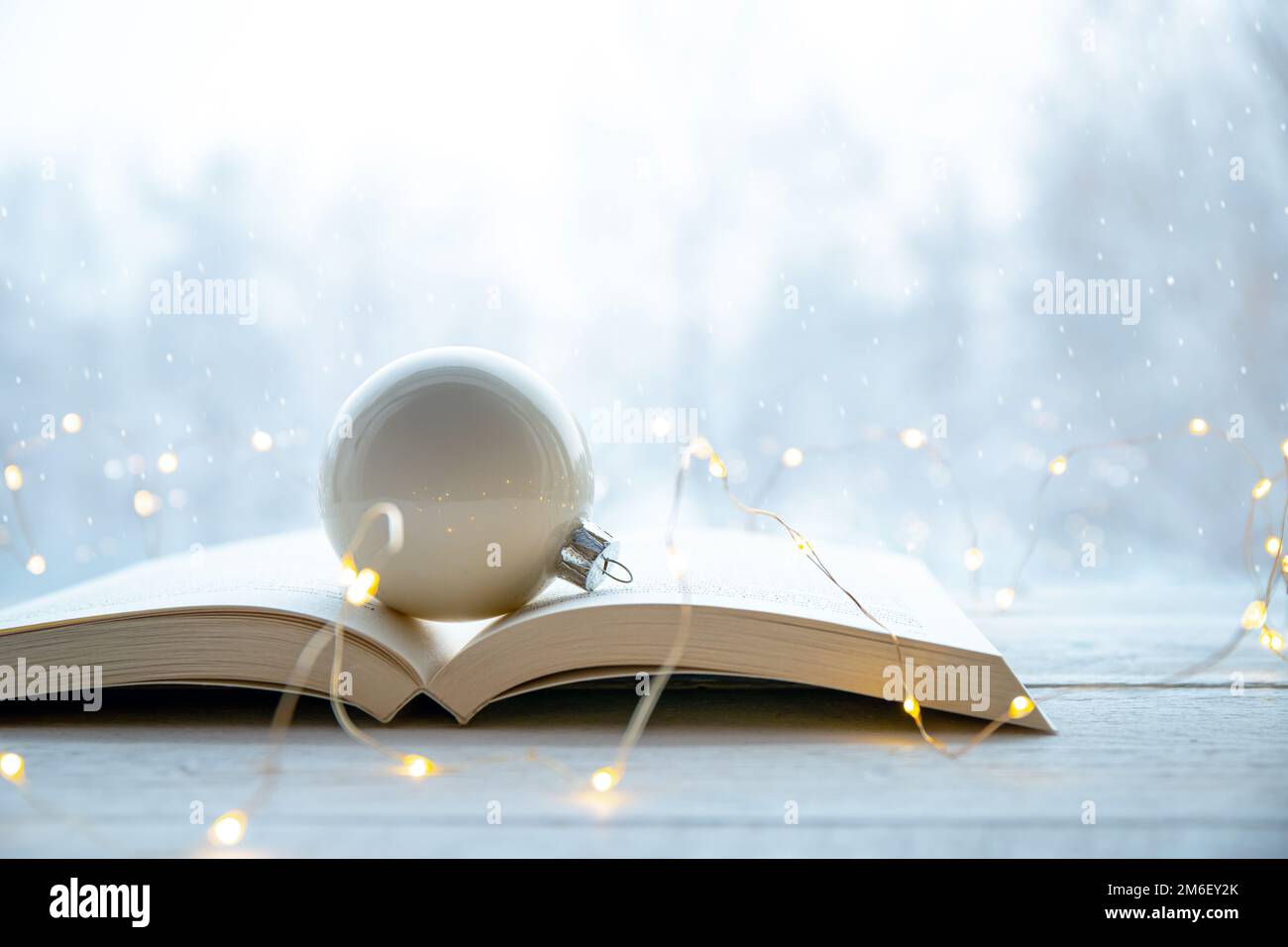 White Christmas bauble on top of open paper book with fairy lights ...