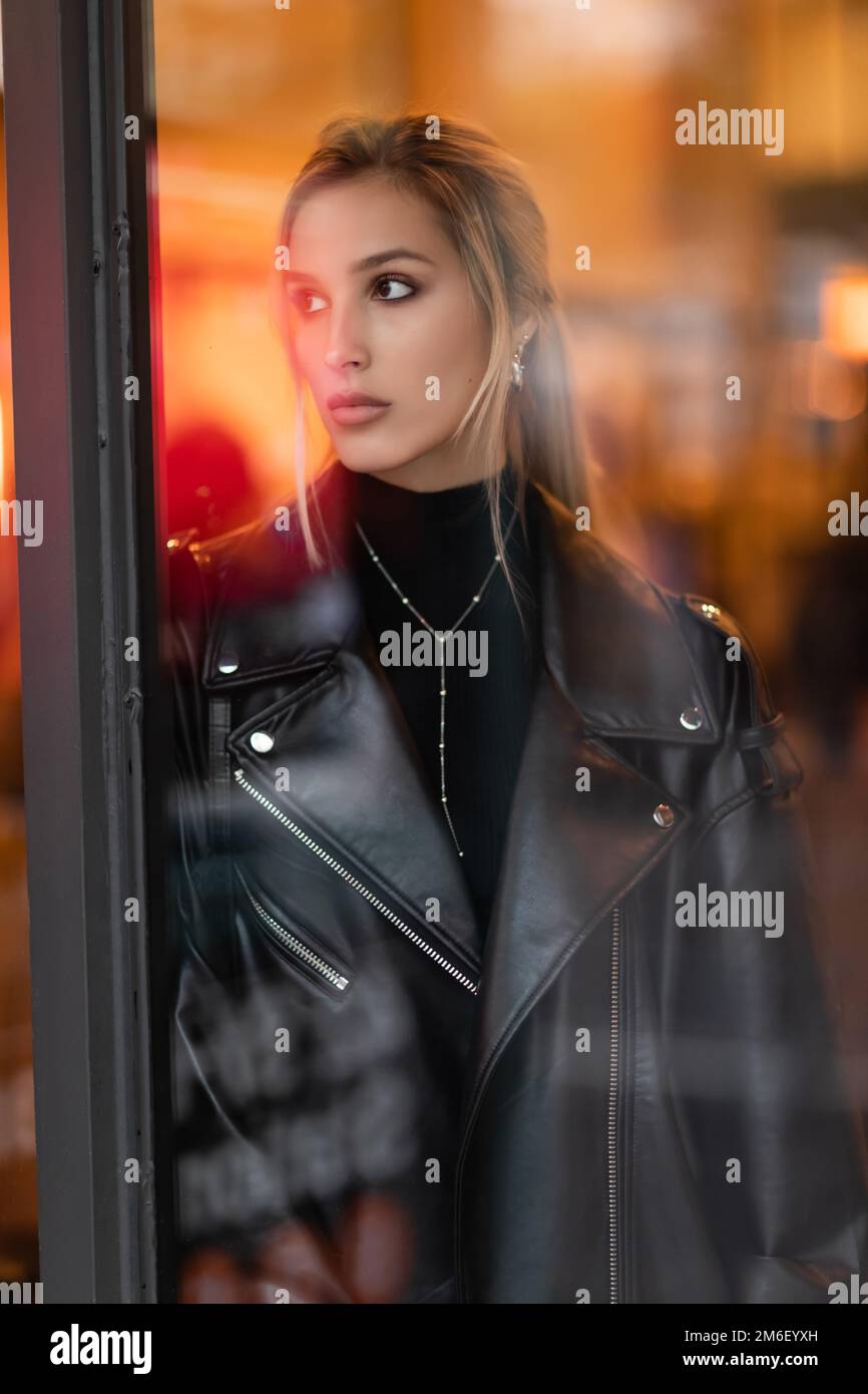 blonde woman in black leather jacket looking through glass window in ...