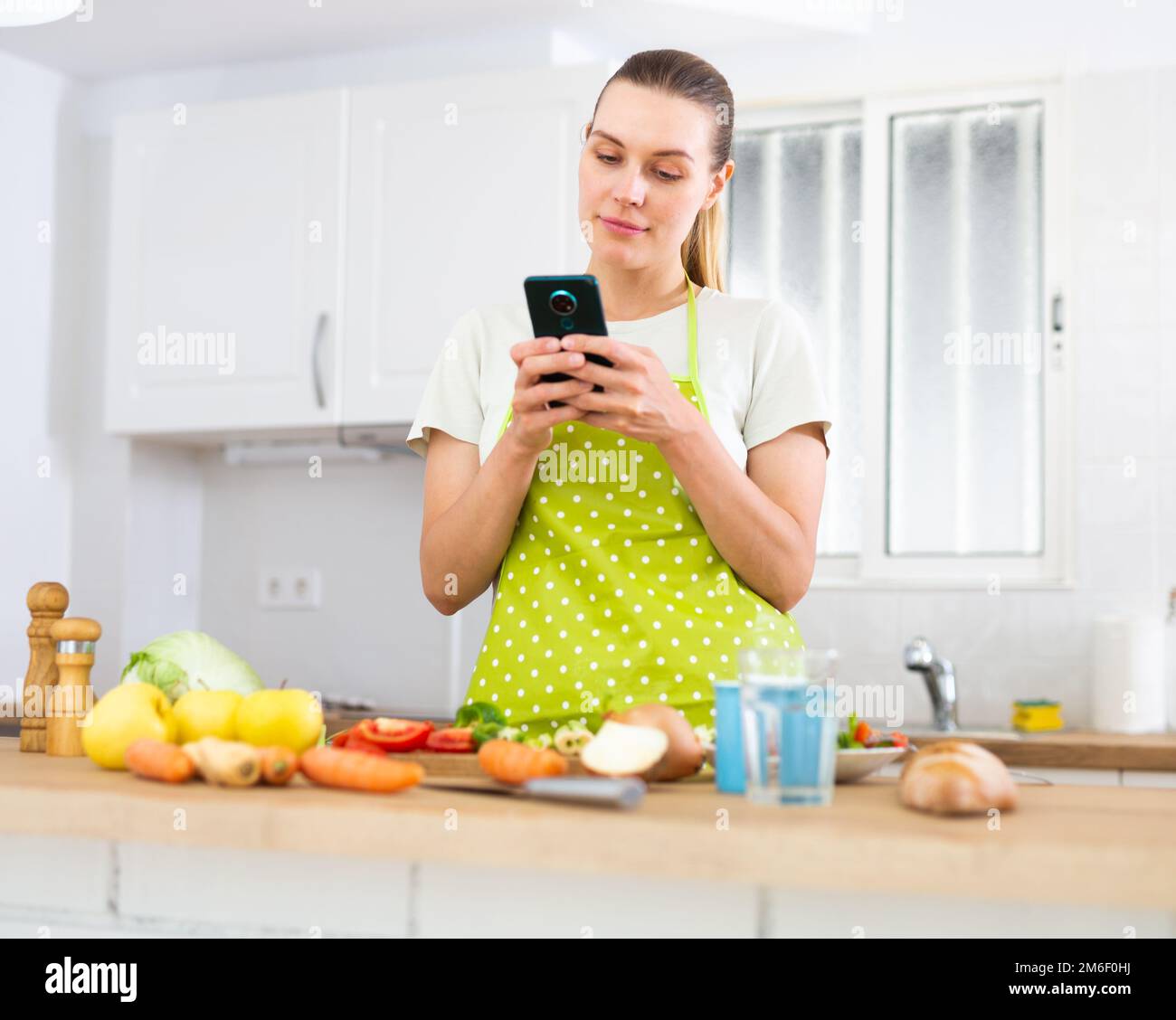 Young housewife using phone to find recipe while cooking dinner Stock ...