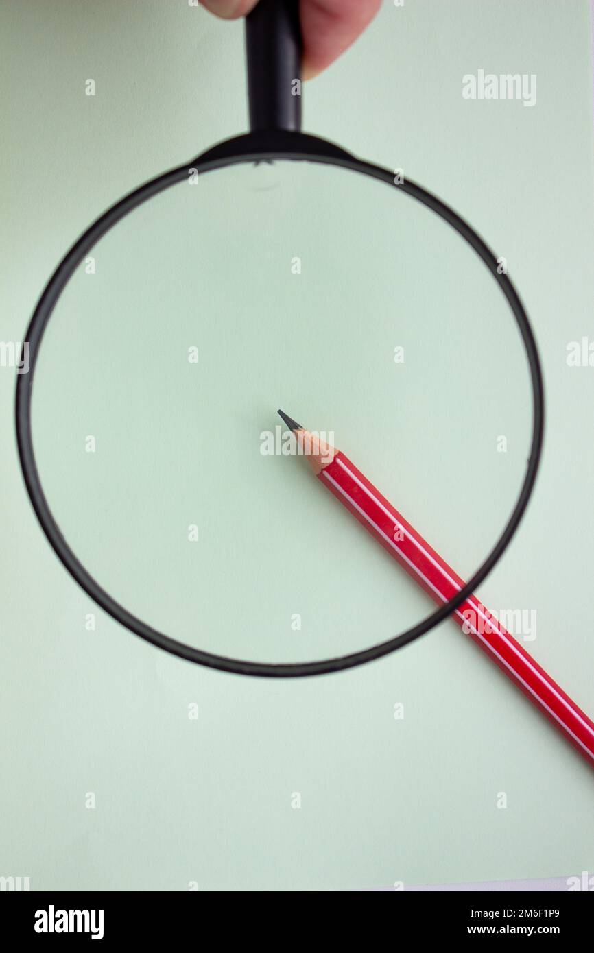 One red pencil under a magnifying glass close-up on a light background ...
