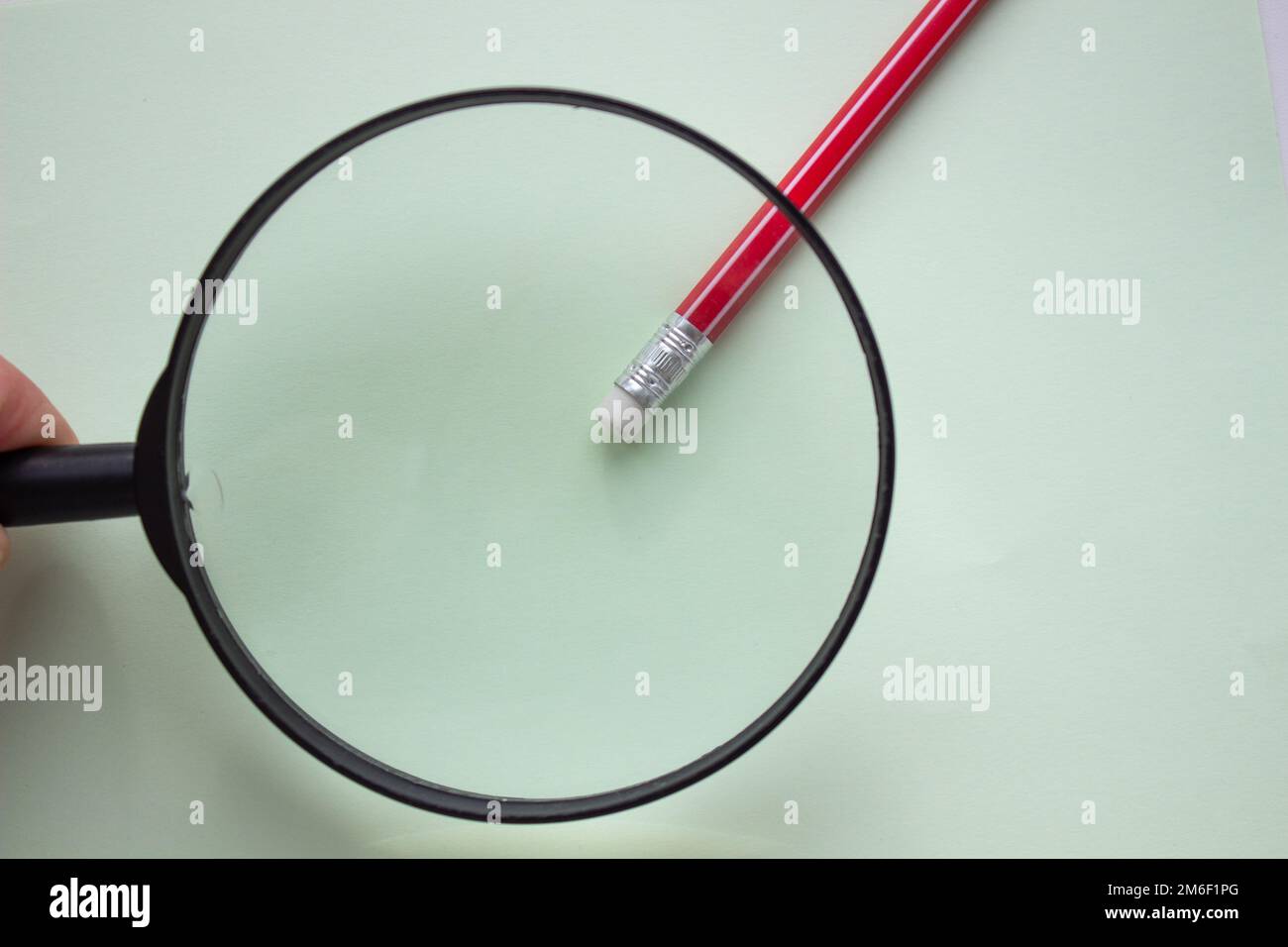 One red pencil under a magnifying glass close-up on a light background ...