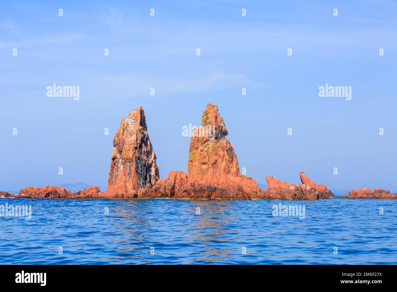A picturesque red stone island sticks out of the blue sea water. An ...