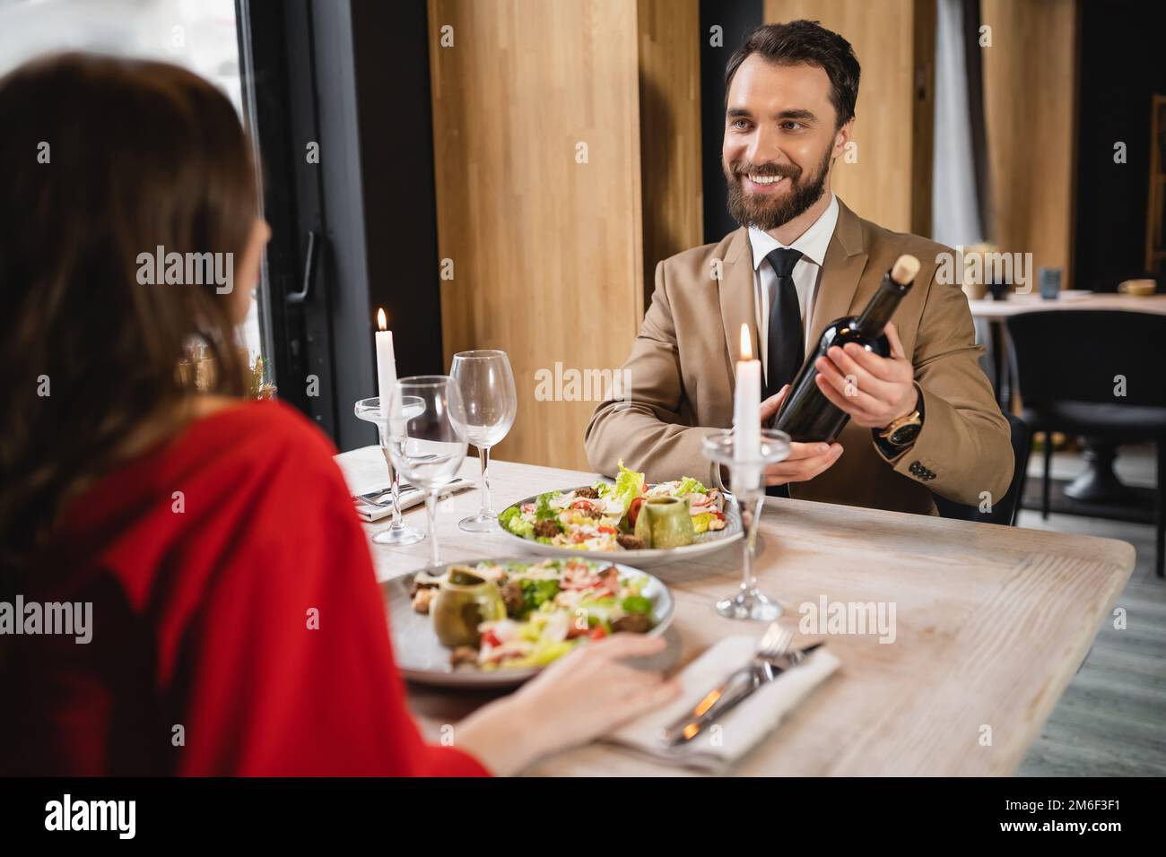 happy man smiling while holding bottle with wine near girlfriend during ...