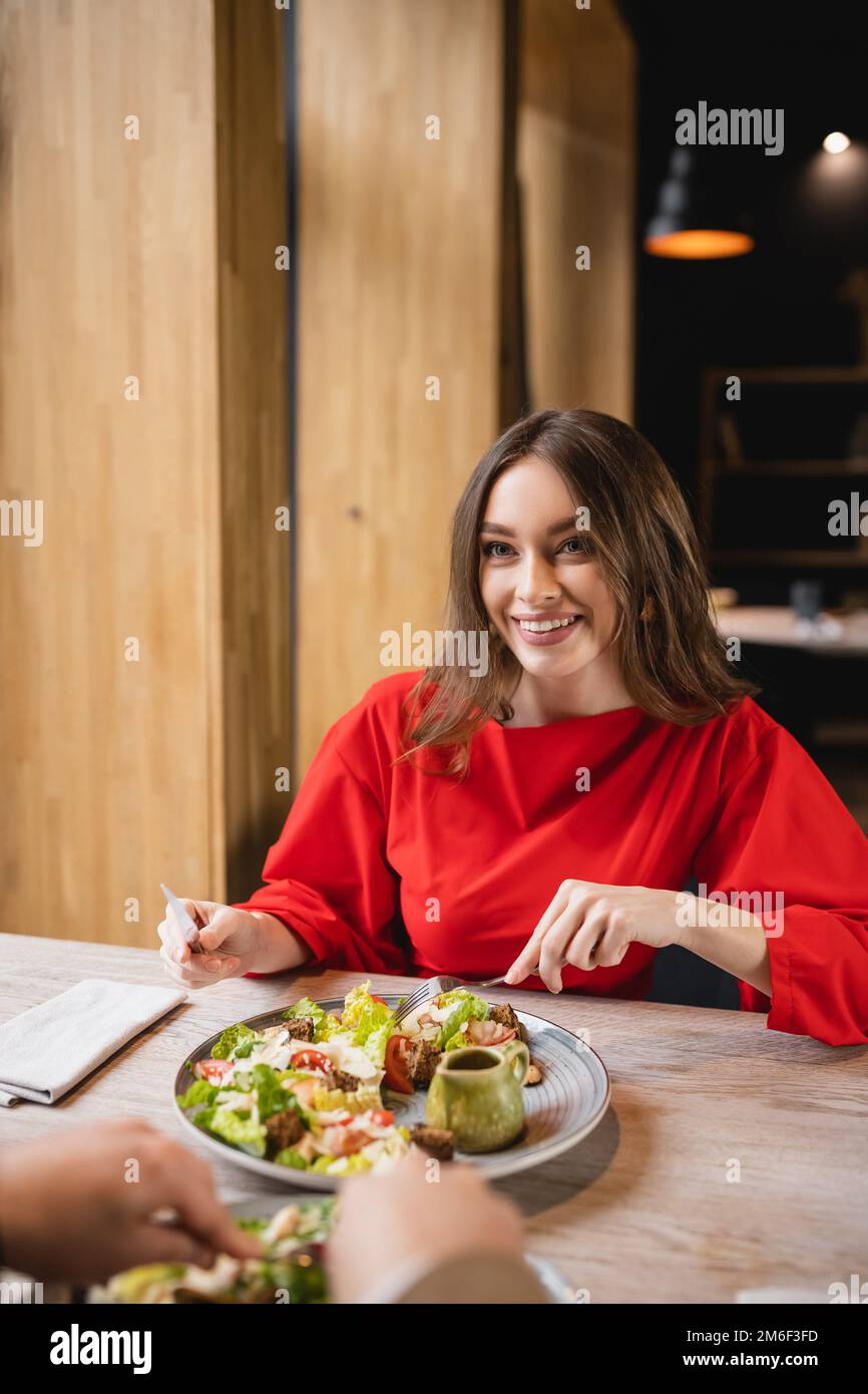 happy woman looking at man in restaurant while holding cutlery near ...