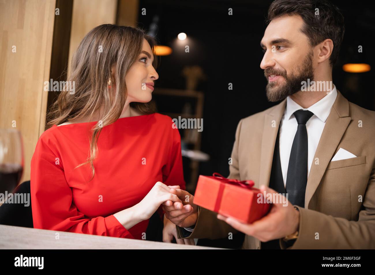 bearded man in formal wear holding present near smiling woman in red ...