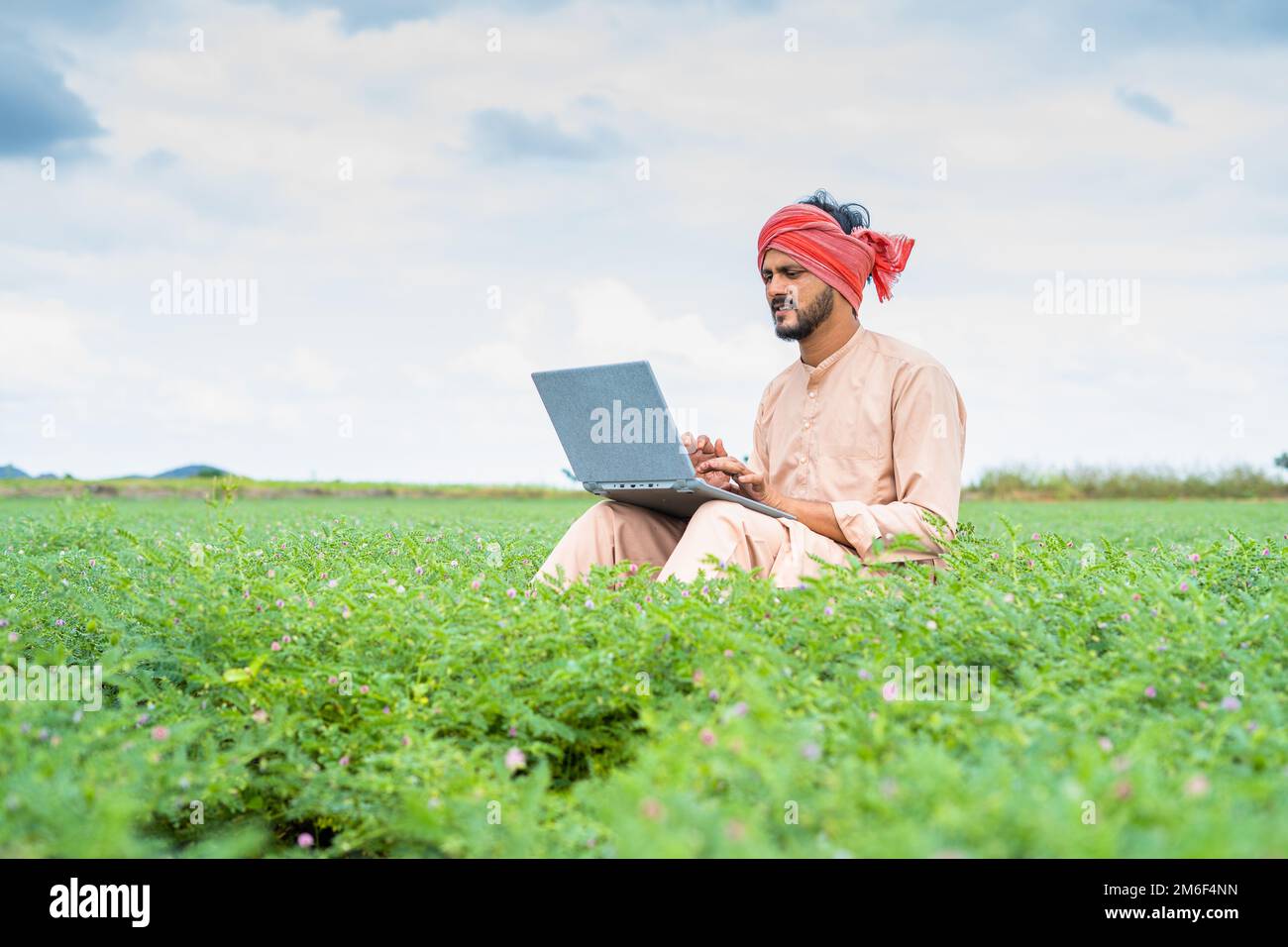 Young indian farmer busy wrking on laptop while sitting at agricultural ...