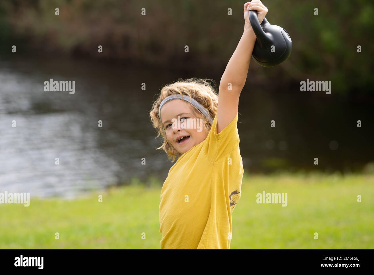 Kid lifting the kettlebell in park outside. Kid boy working out with ...
