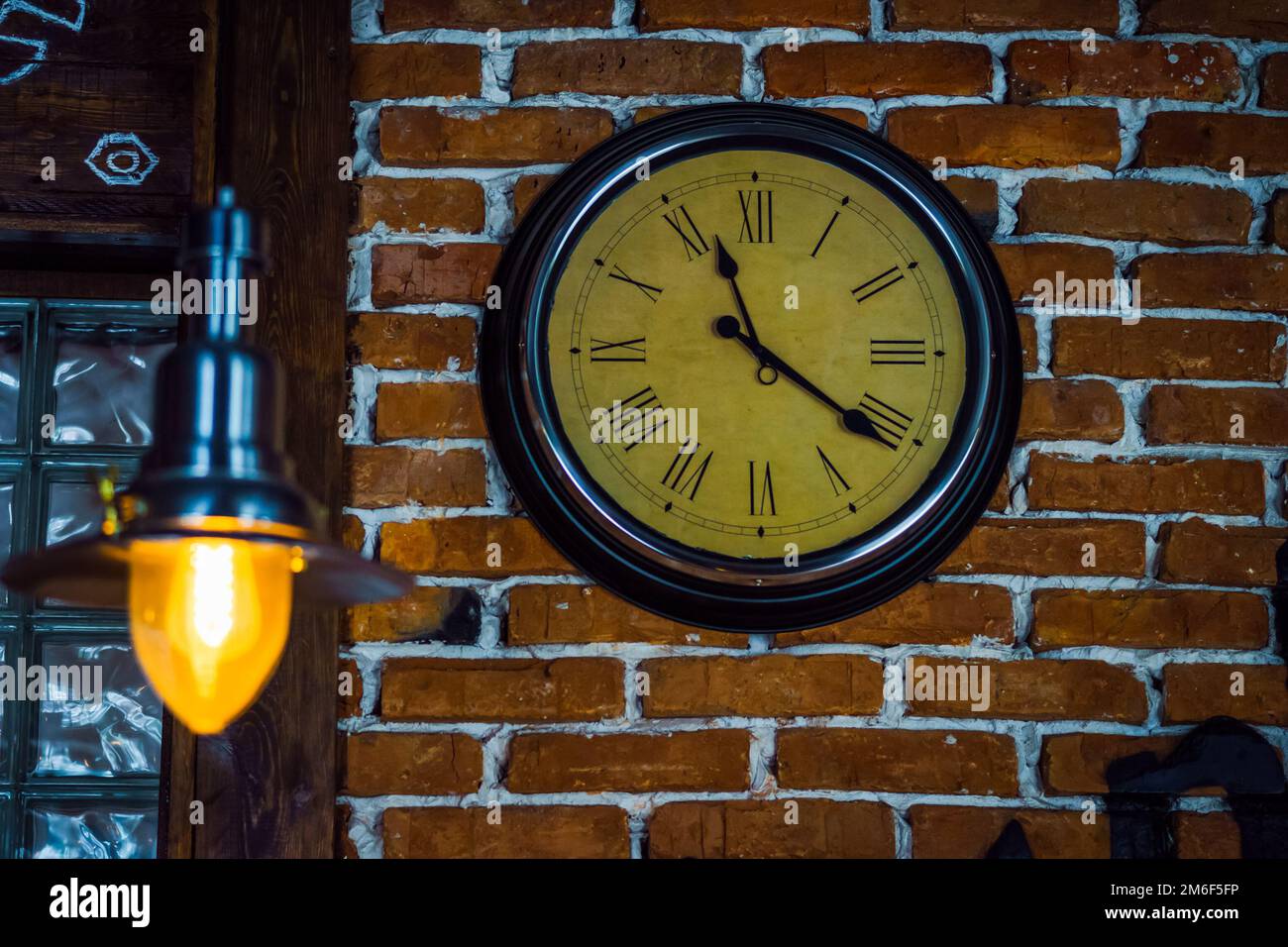 Round clock with Roman numerals hang on brick wall Stock Photo - Alamy